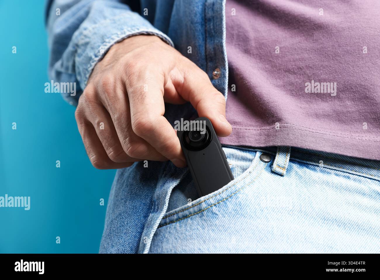Man with hidden spy camera in his pocket on light blue background ...