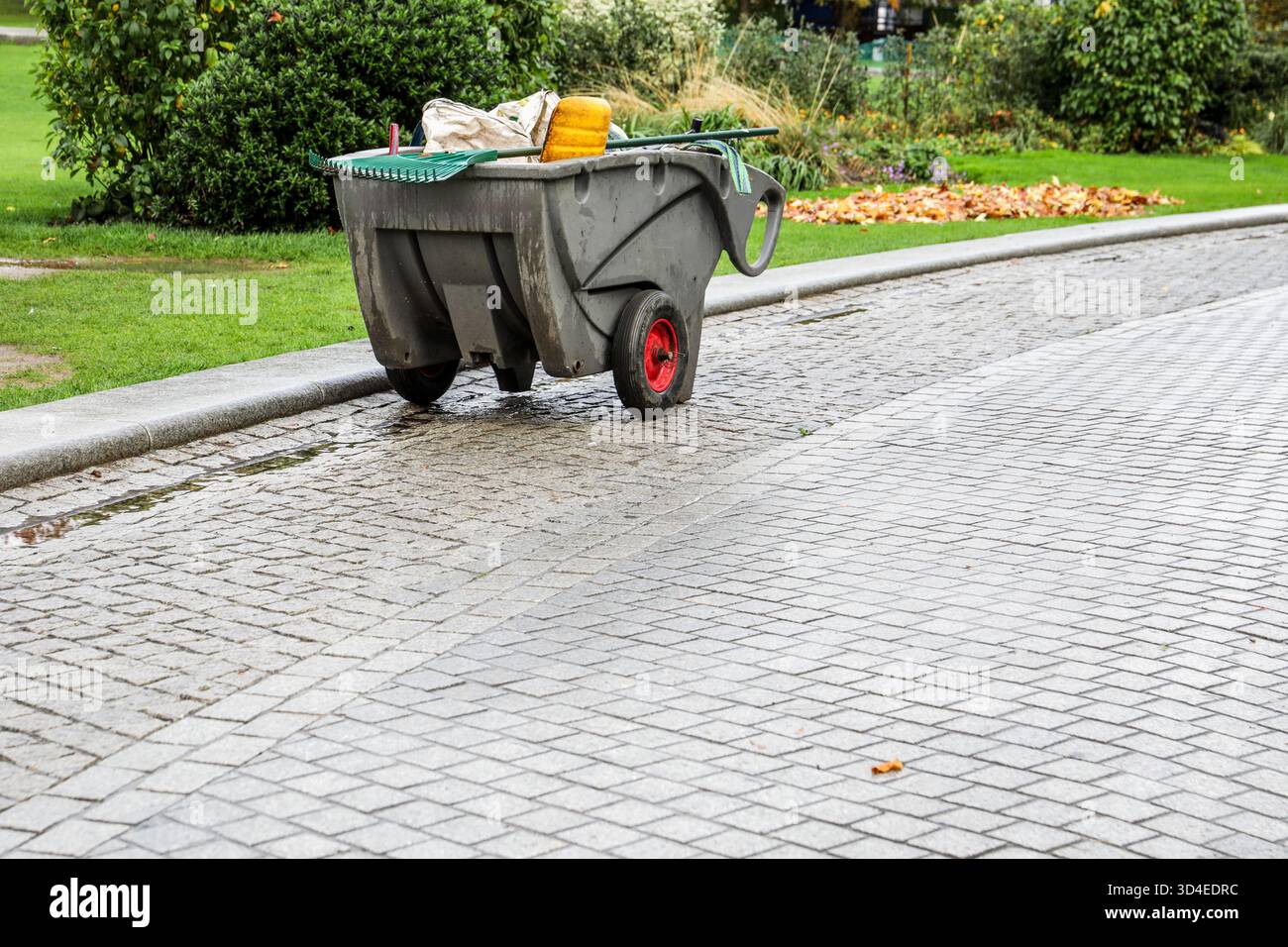 Garden maintenance cart with tools on wet cobblestone path in public ...