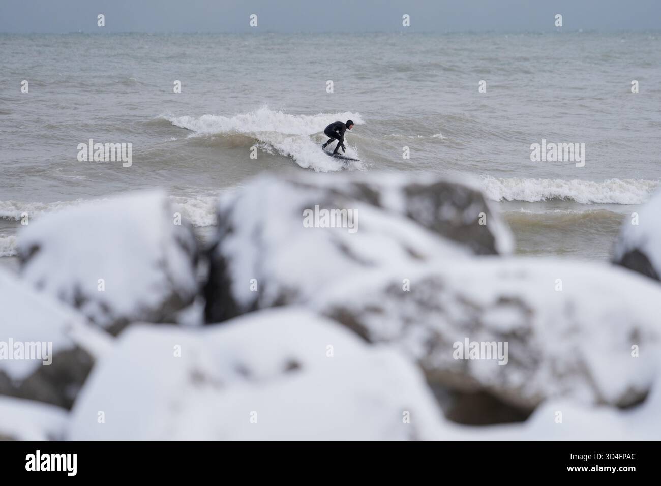A surfer catches a wave as snow covers the ground n Evanston, Ill., a ...