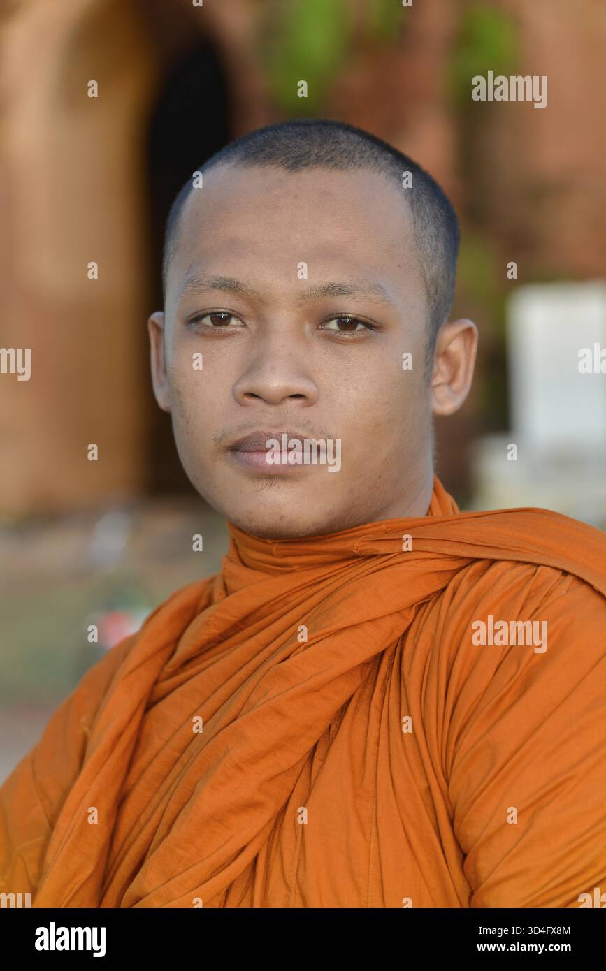 Portrait of a serious looking monk in orange robe in front of a temple ...