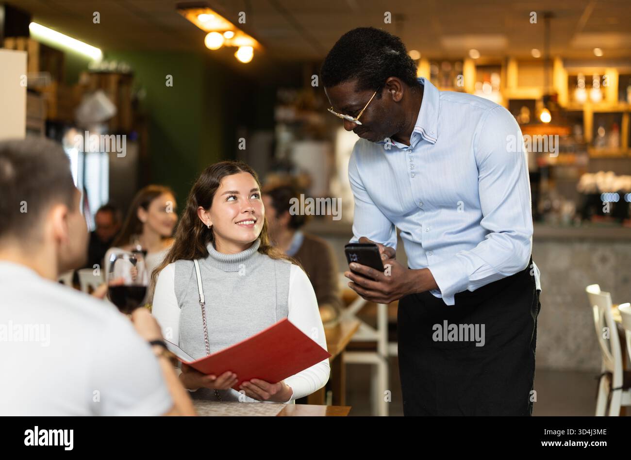 African male waiter communicates with female customer, serve couple in ...