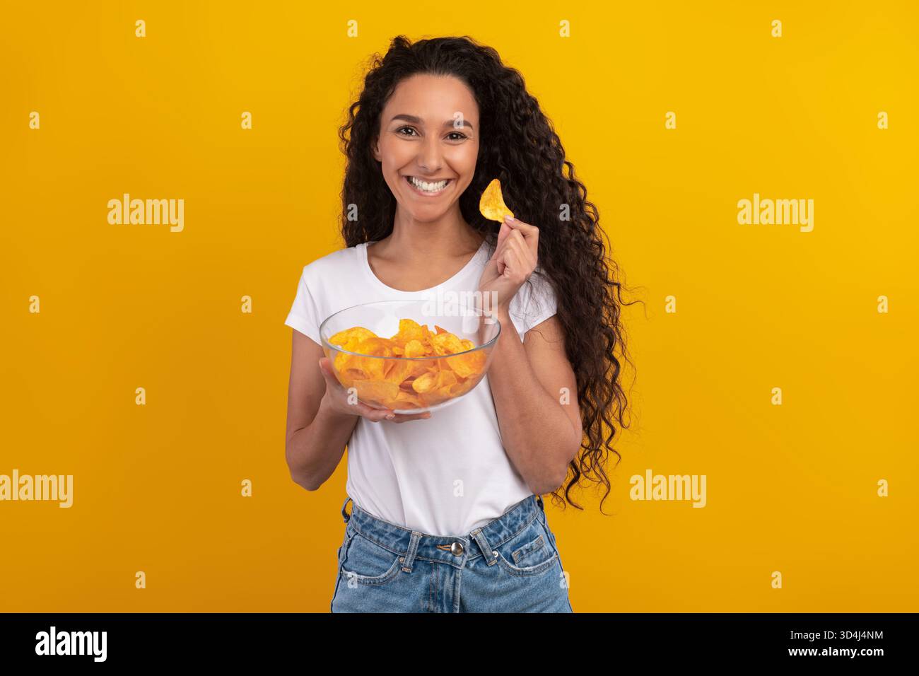 Excited Latin Lady Enjoys Tasty Potato Crisps in Bright Yellow Studio ...