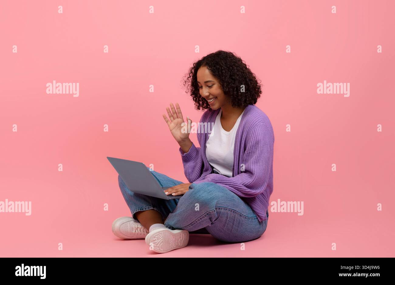 Young Black Woman Enjoys Video Chat While Sitting Cross Legged on Pink ...