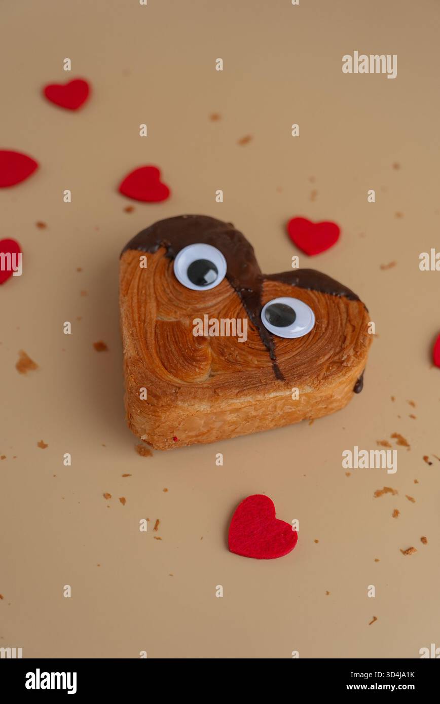 Funny creative eyes on Heart shaped dark chocolate croissant on beige ...