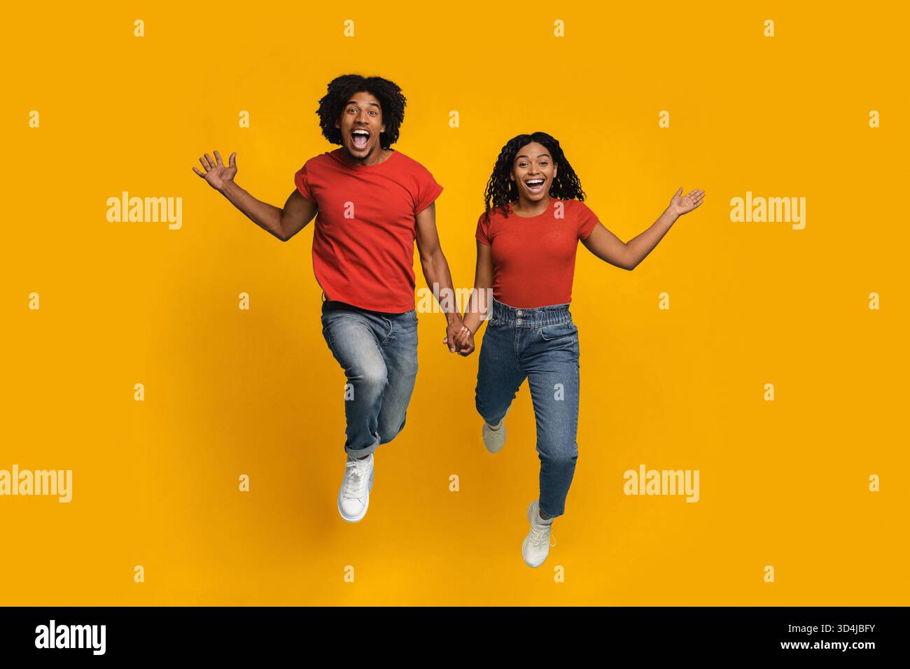 Joyful Couple Jumping Together Against a Bright Yellow Backdrop Stock ...