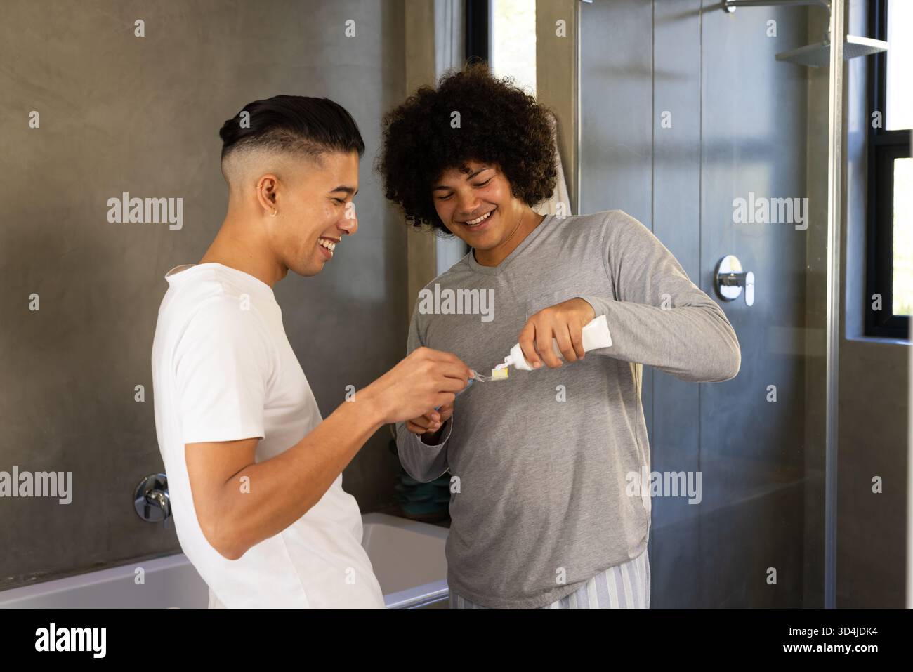 Smiling Diverse male couple brushing teeth together in bathroom with ...