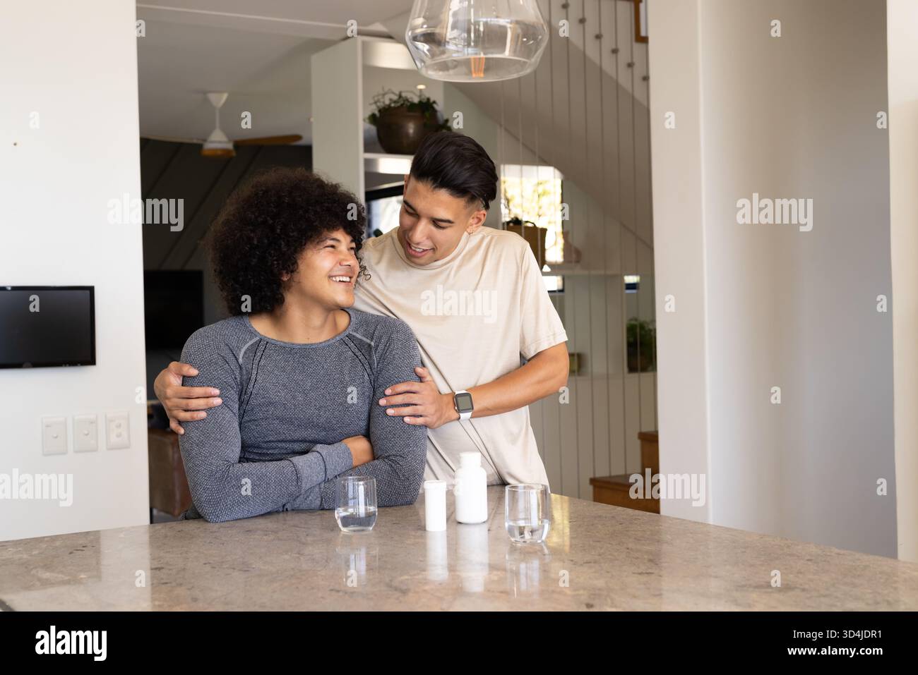Smiling Diverse male couple hugging at kitchen countertop island, with ...