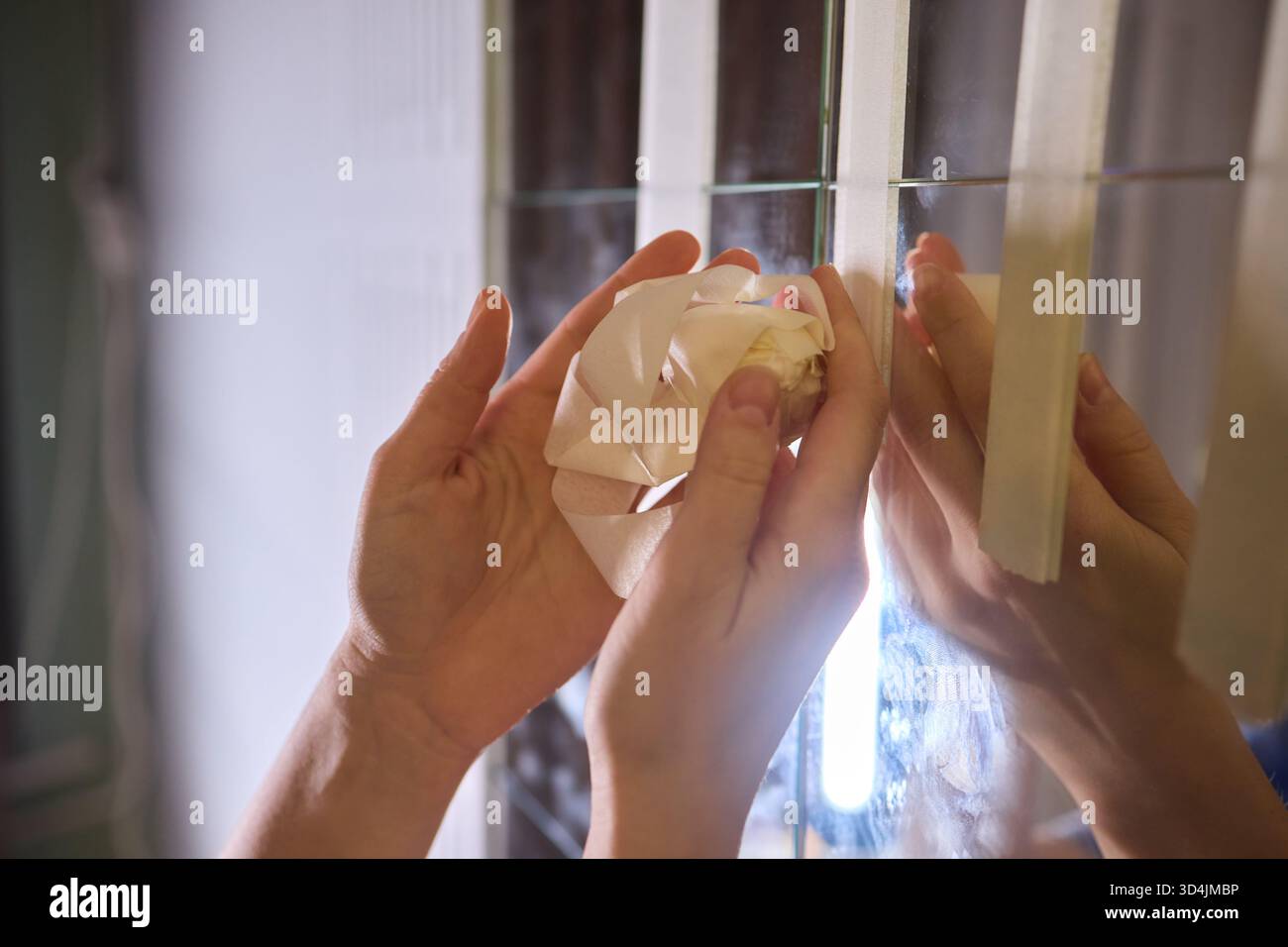Hands smoothing tape edge on mirror, final finishing touch during home ...