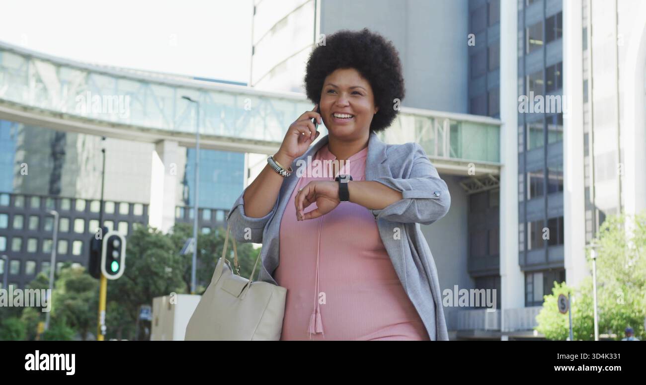 Smiling professional woman checking smartwatch and talking on phone by ...