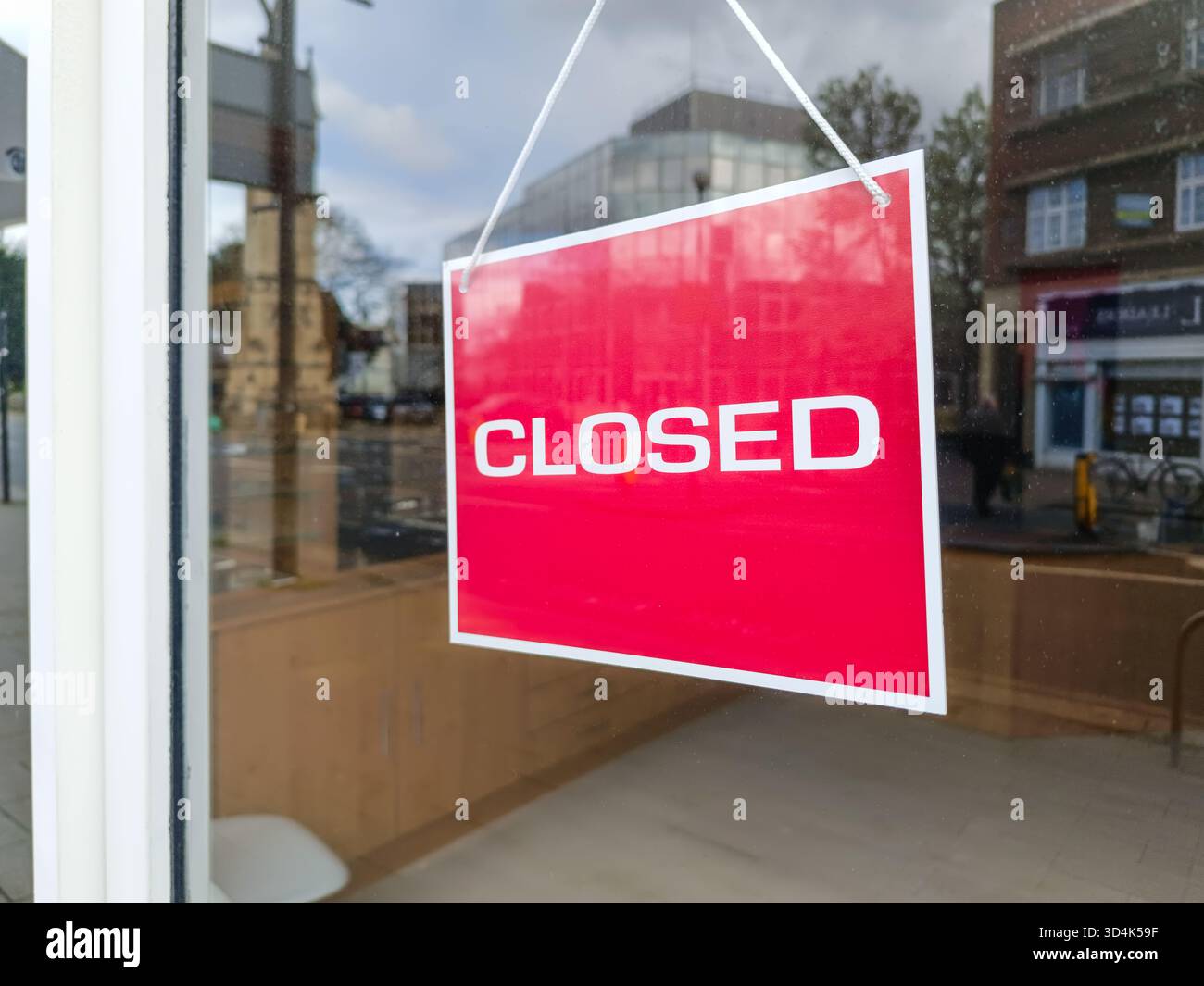 Red 'Closed' sign on a glass door of a small retail shop. Empty interior and reflections suggest ...