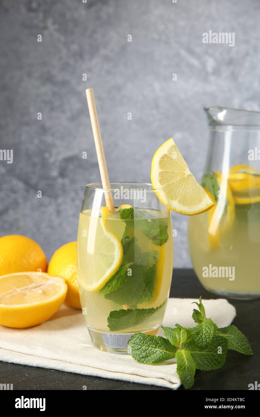Fresh lemonade in glass, jug, lemons and mint on black table, closeup ...