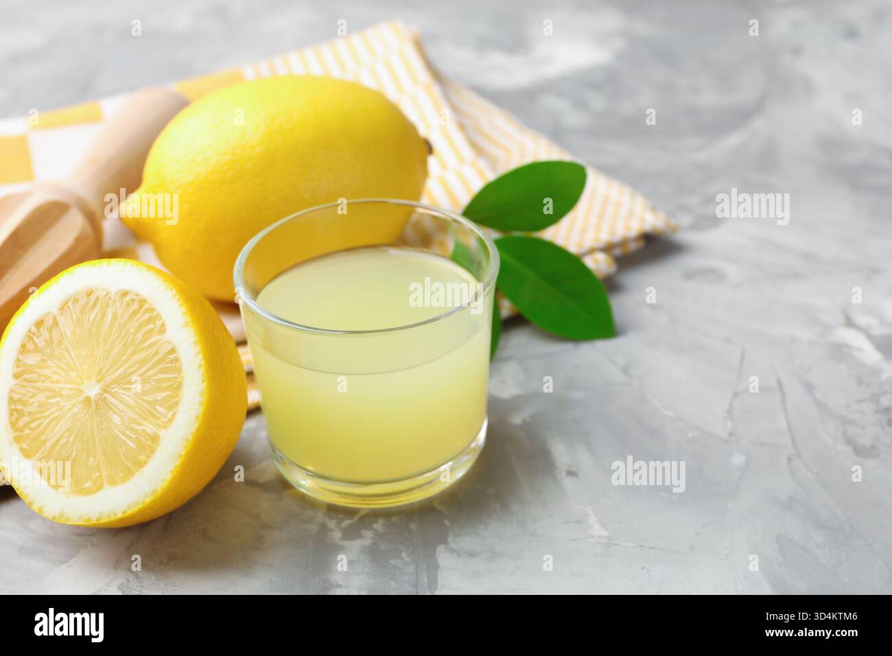 Lemon juice in glass, squeezer, leaves and fresh lemons on light grey ...