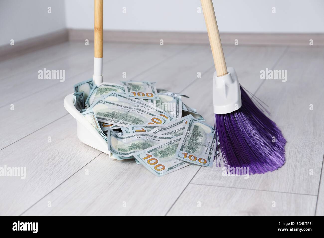 Sweeping dollar banknotes with broom into dustpan on light wooden floor ...
