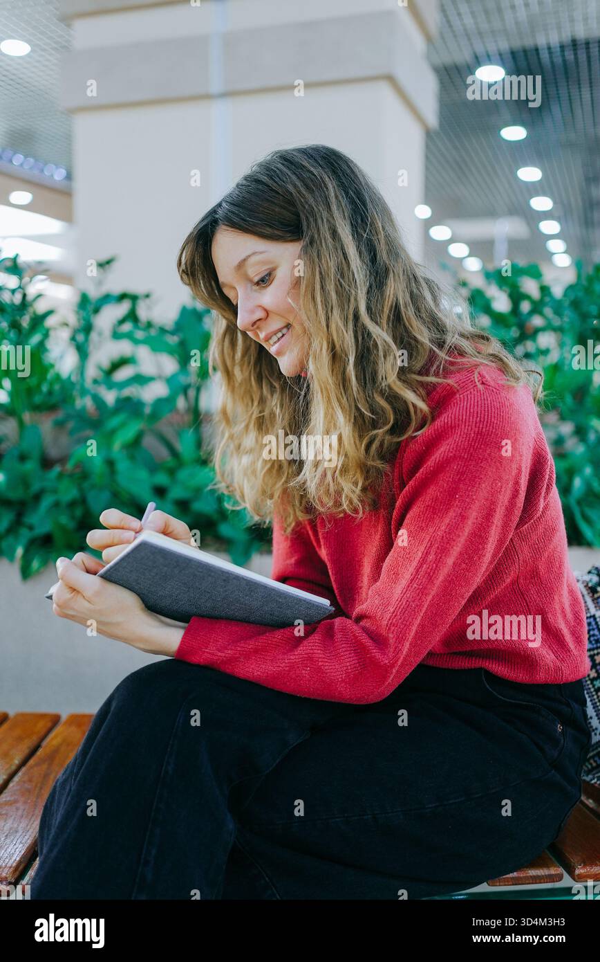 Young woman writing notes and journaling in a gray notebook with a pen ...