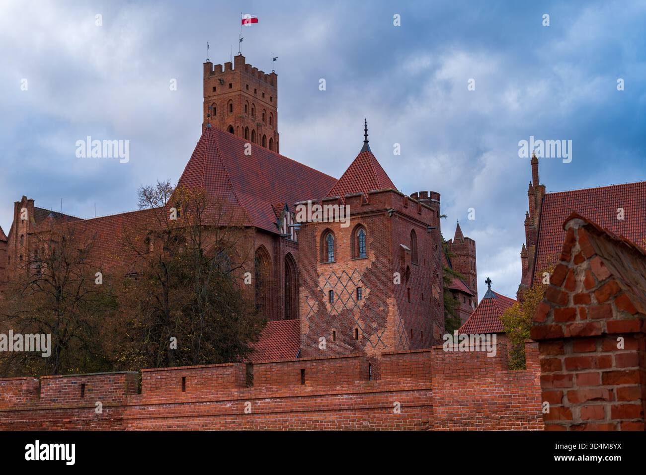 Malbork Castle in Malbork, Poland rises behind walls with a flag on a ...
