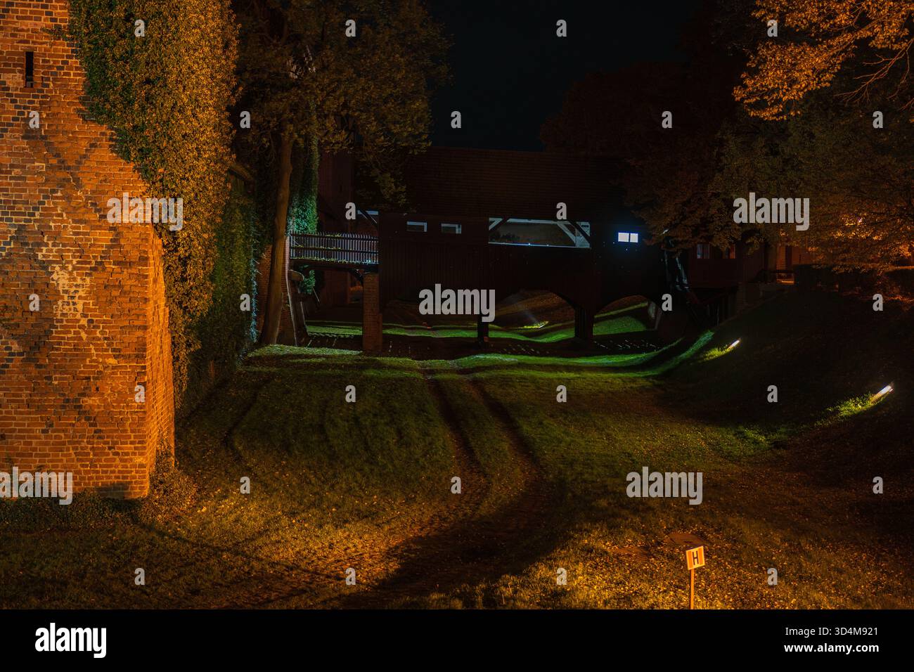 Warm amber light grazes red Gothic brick and ivy as cool green uplights ...