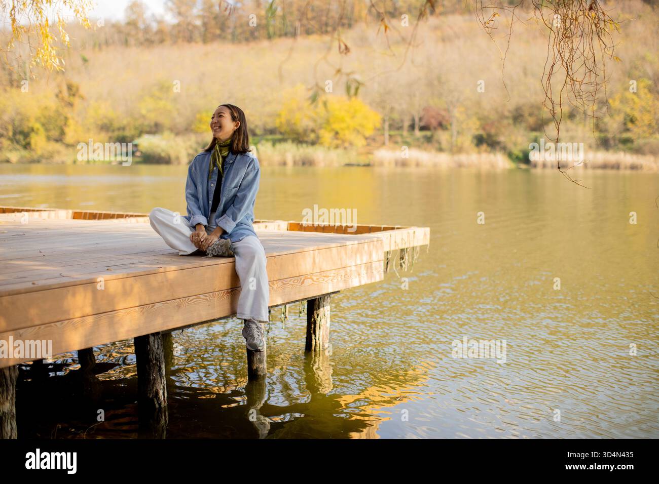 A woman sits calmly on a wooden dock, smiling peacefully as she enjoys ...