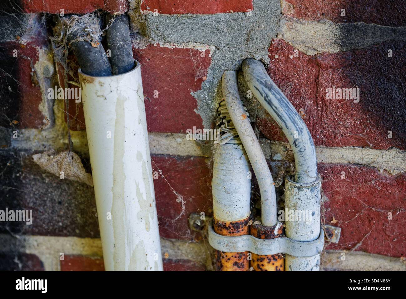 An old concrete wall holds cracked pipes and loose cables that push out ...