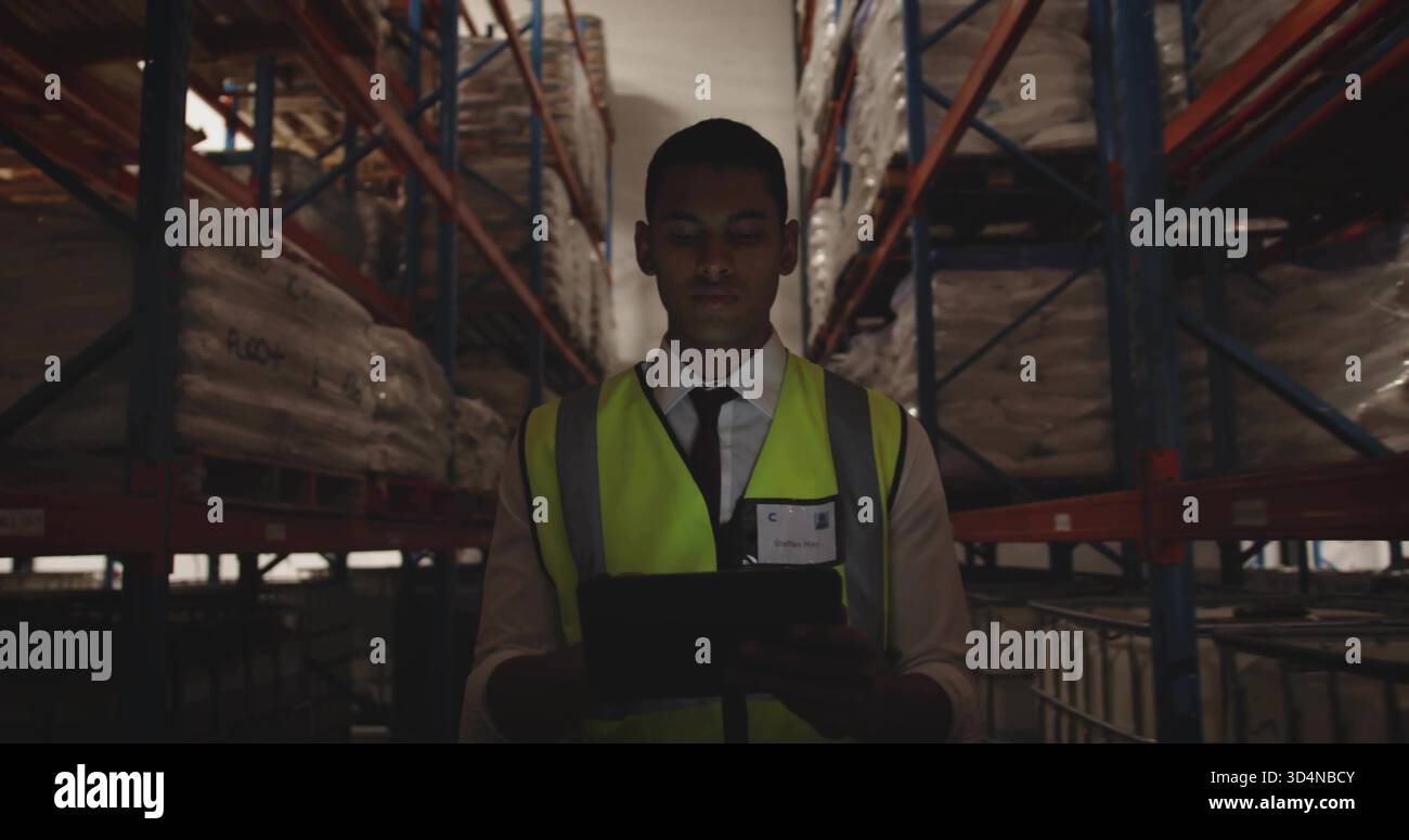 Inspecting man holding tablet checking stock in warehouse aisle, in ...