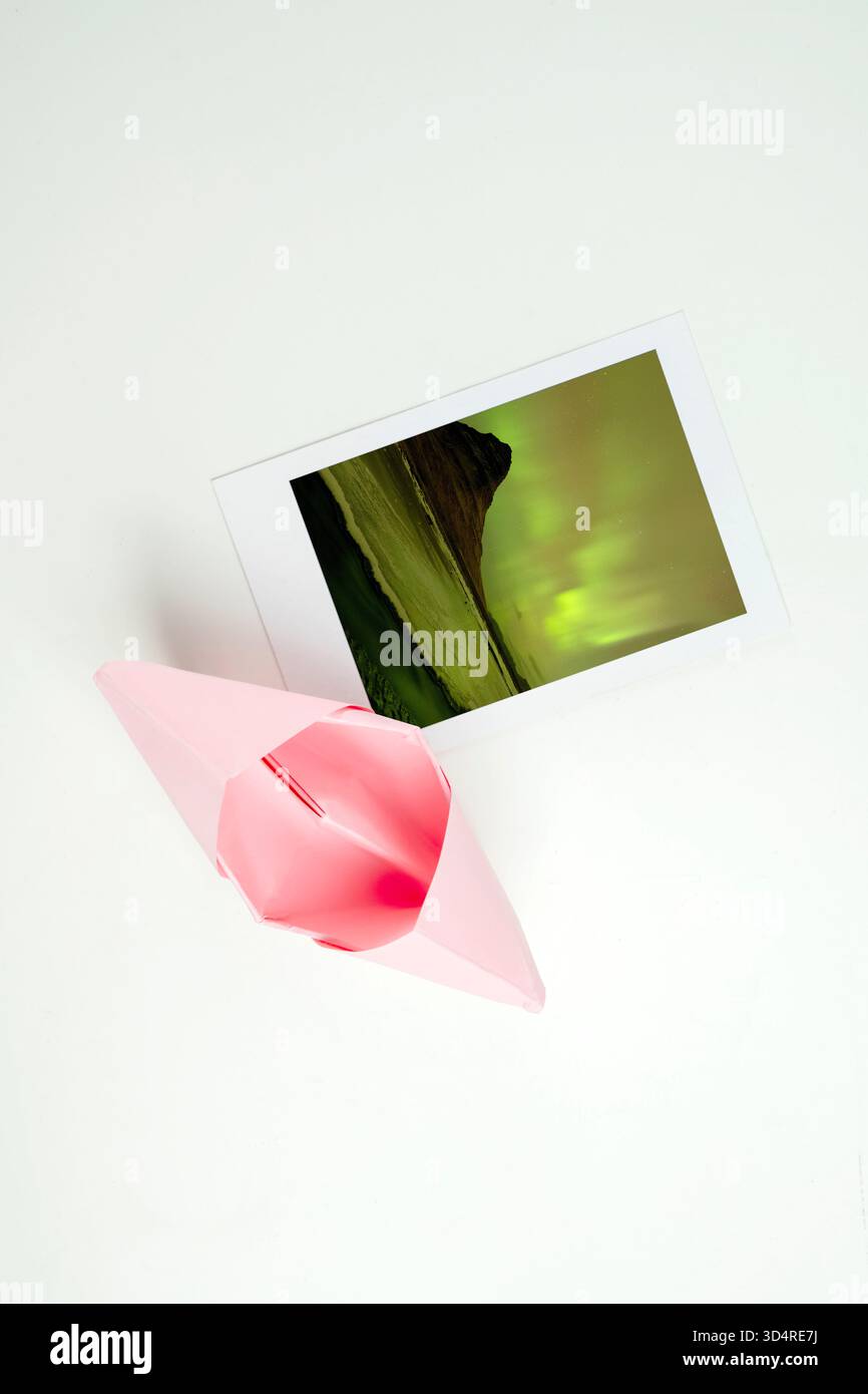 Pink paper boat and instant print of aurora isolated over a white ...