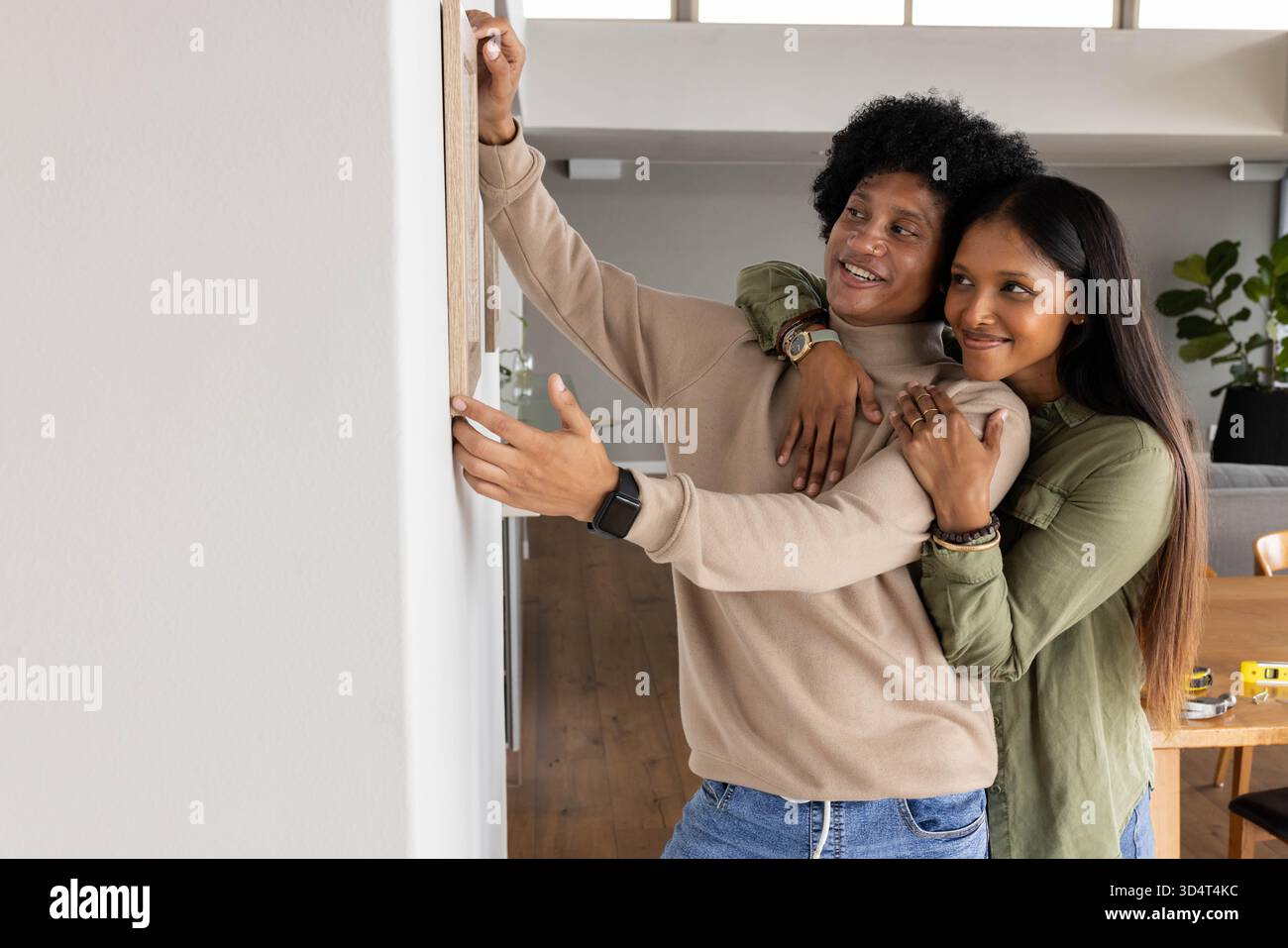 Hanging diverse couple aligning wooden frame on white wall, with spirit ...