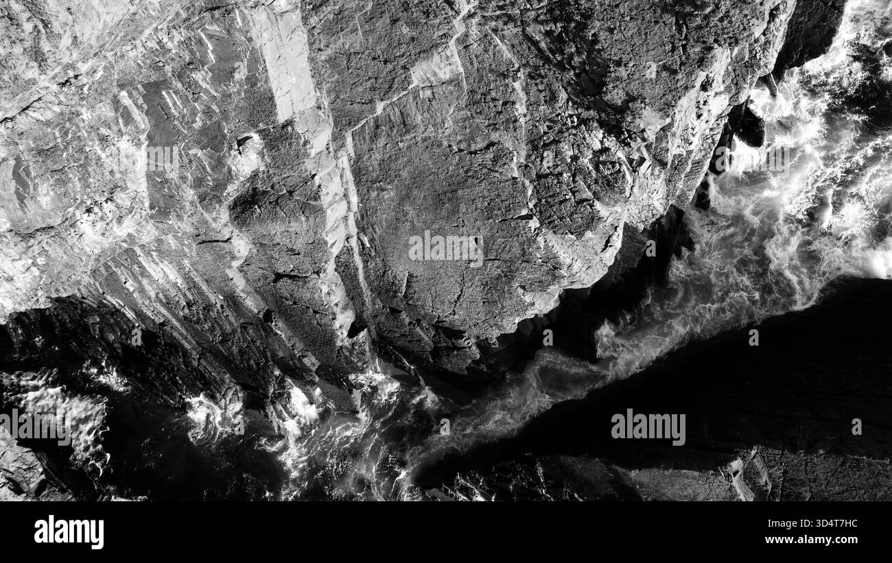Aerial black and white view of rugged coastal cliffs with waves below ...