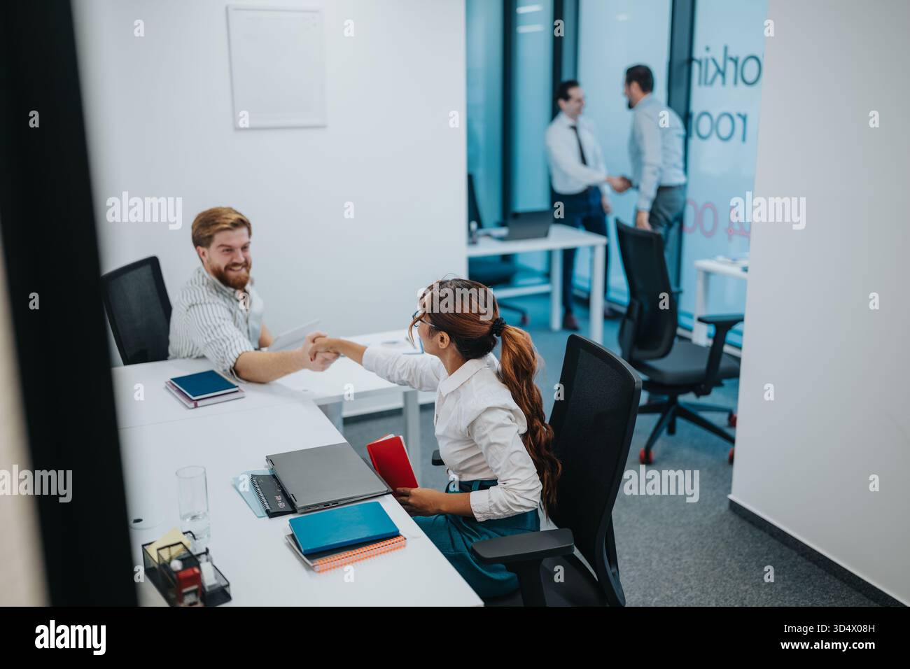 Office scene with handshake between colleagues at a desk during a ...