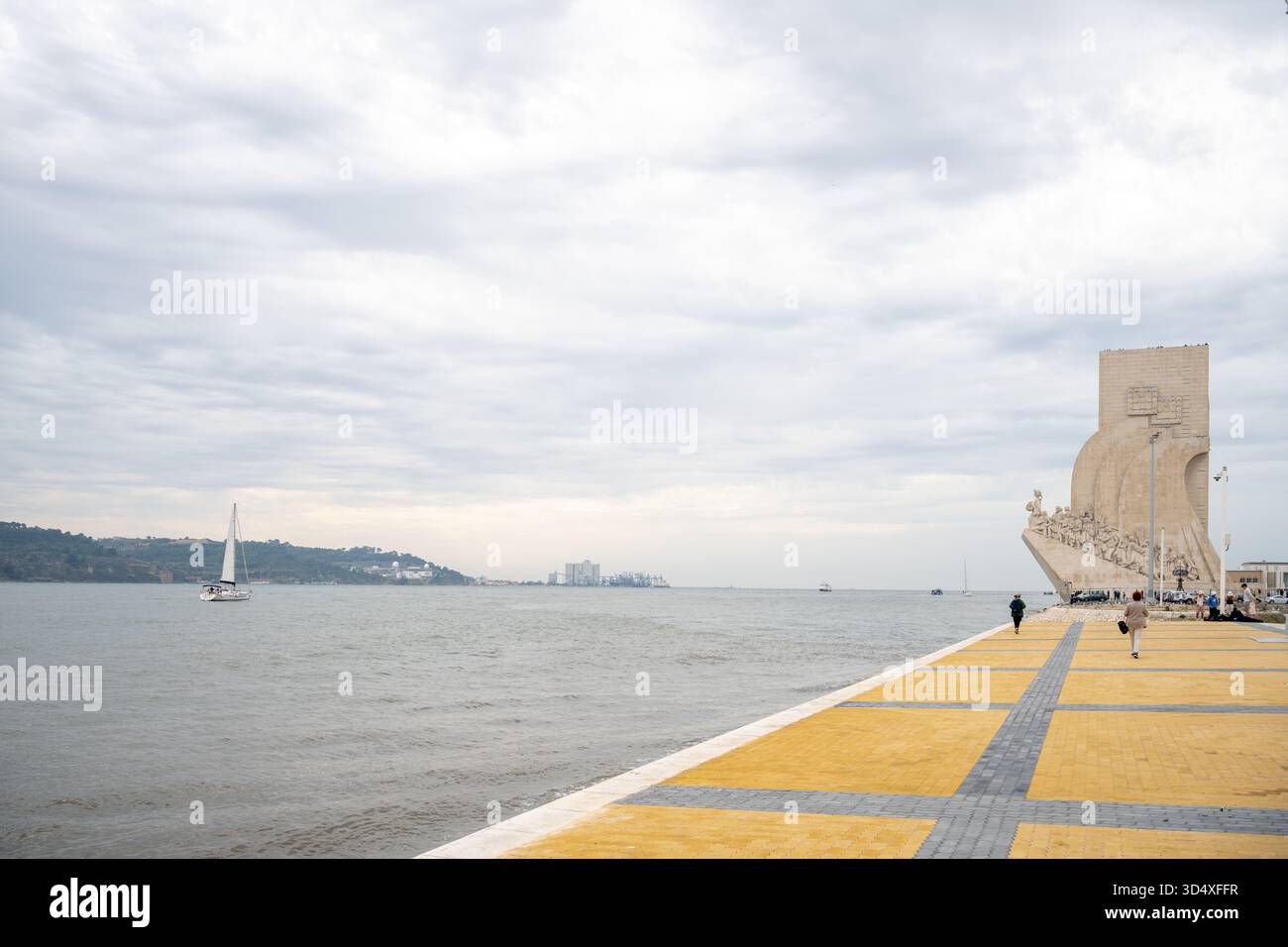 People walking along the yellow-tiled waterfront promenade with the ...