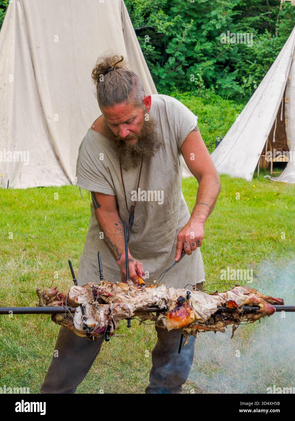 Bøstad, Norway - August 3, 2023: Man in medieval folk costumes roast a ...
