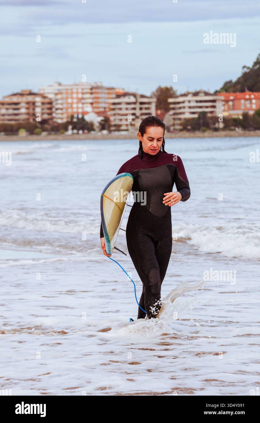 Female surfer holding board while exiting the ocean on a city beach ...