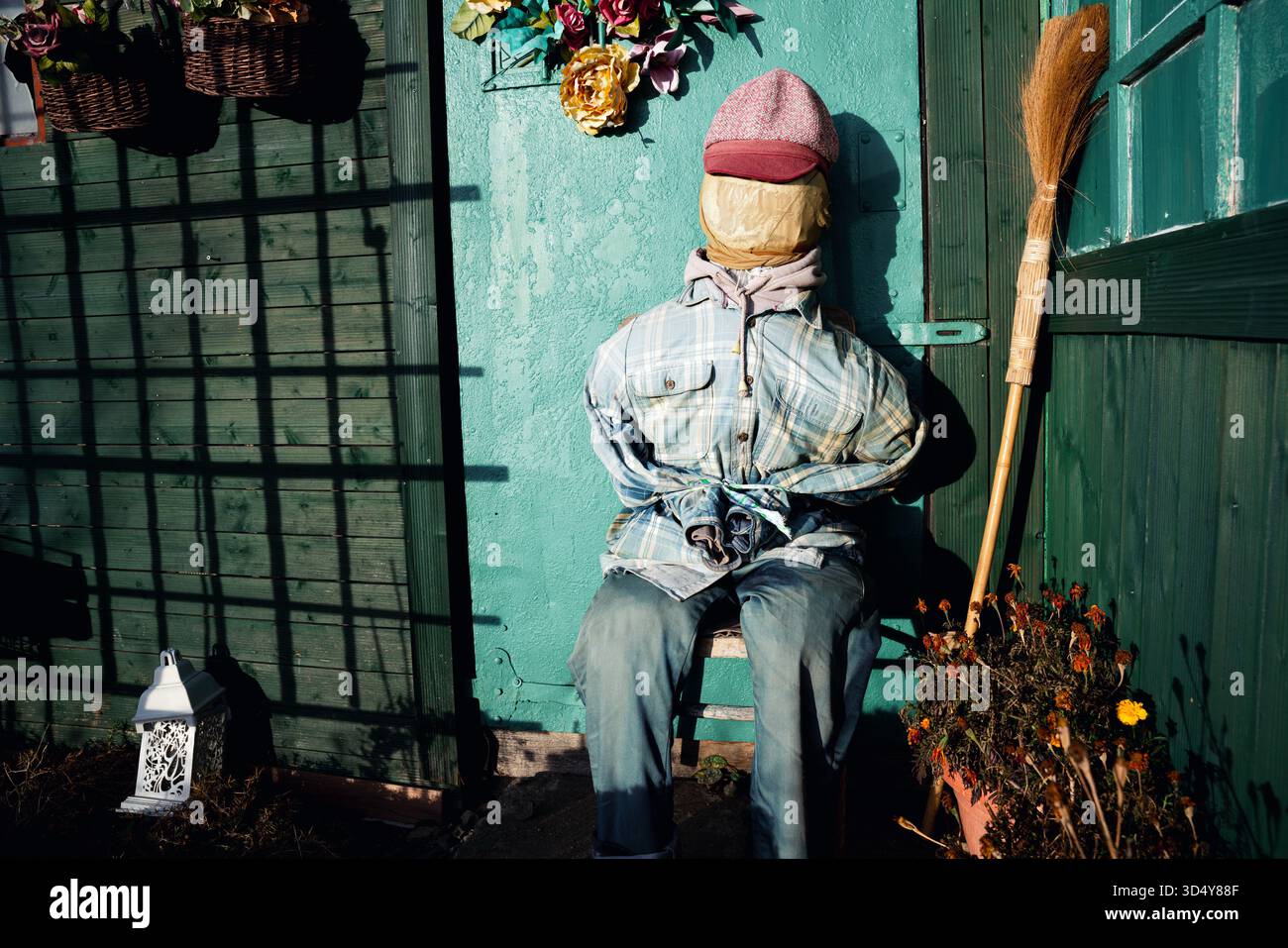 A scarecrow sitting on a wooden chair in front of a small garden gazebo ...