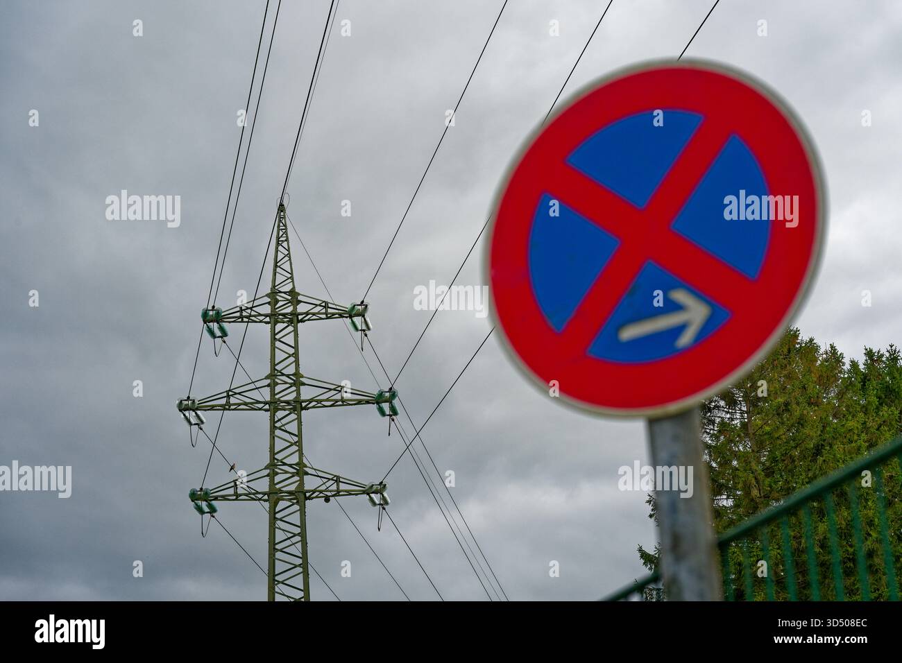 A steel utility pylon stands by the street and holds long electric ...