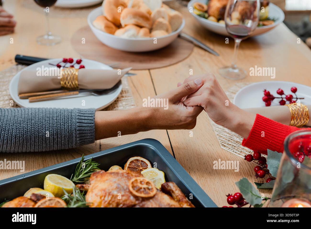 Diverse couple holding hands across wooden dining table with roasting ...