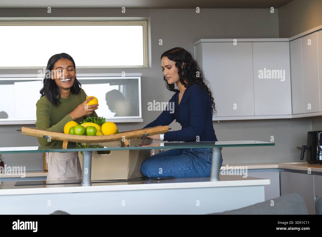 Diverse female friends arranging lemons and apples at glass kitchen ...