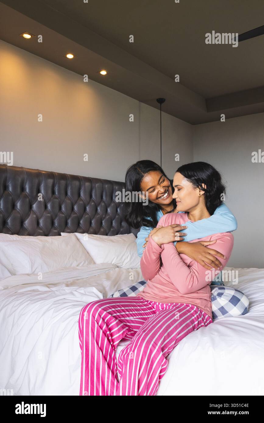 Hugging diverse female partners sitting on bed in modern bedroom, with ...