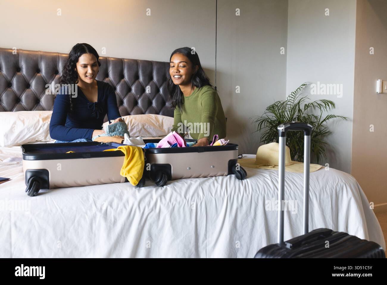 Packing diverse female friends folding colorful clothes on bed at hotel ...