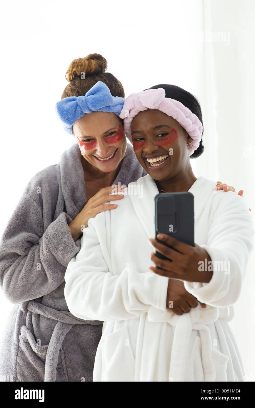 Holding smartphone, Diverse female friends posing in bright spa area ...