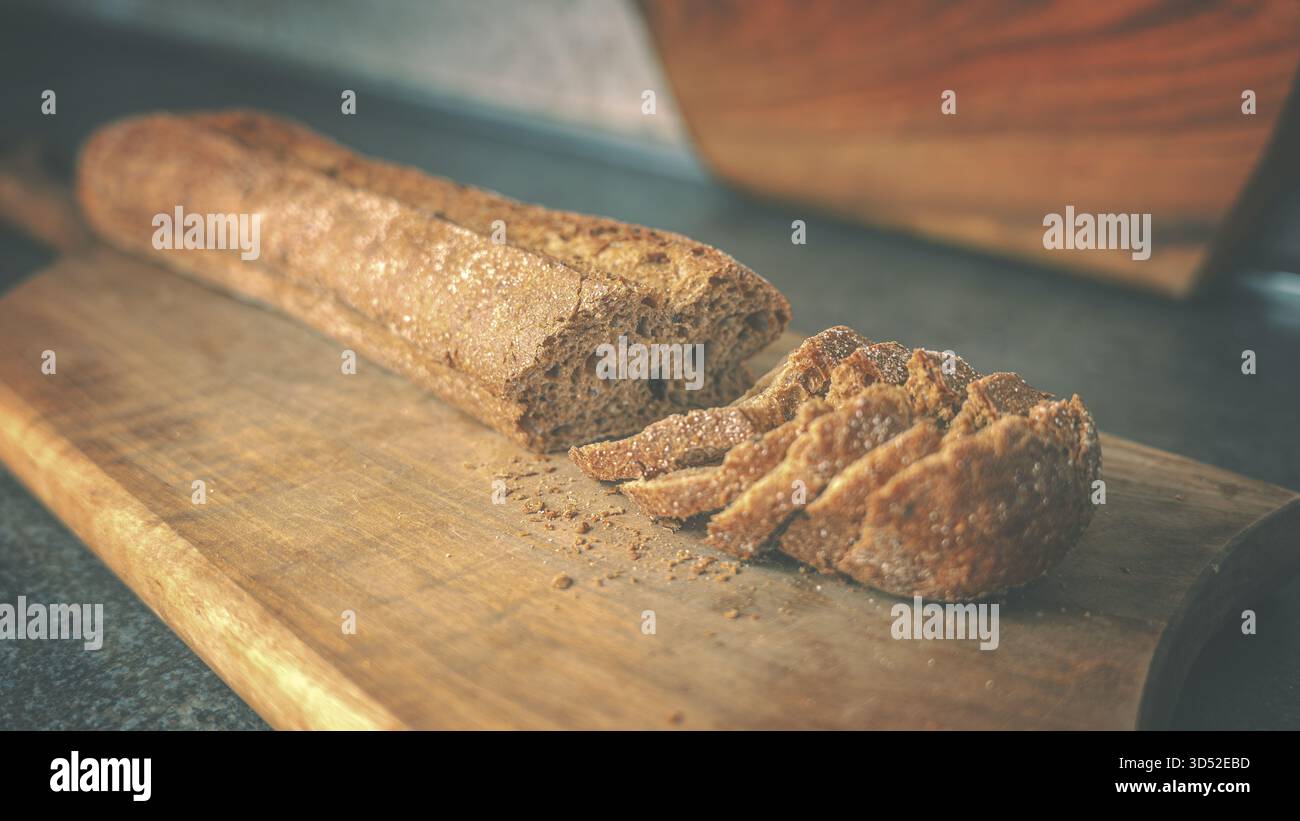 Dark artisan bread baguette positioned on a wooden board on a table ...
