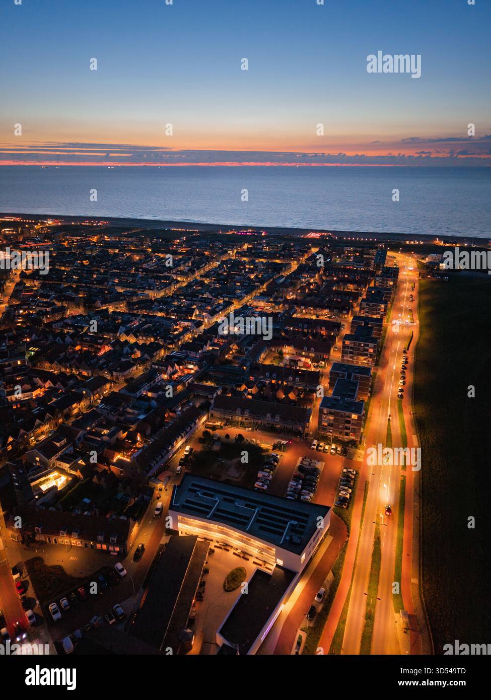 Aerial dusk view of coastal town warm streetlights trace diagonal road ...