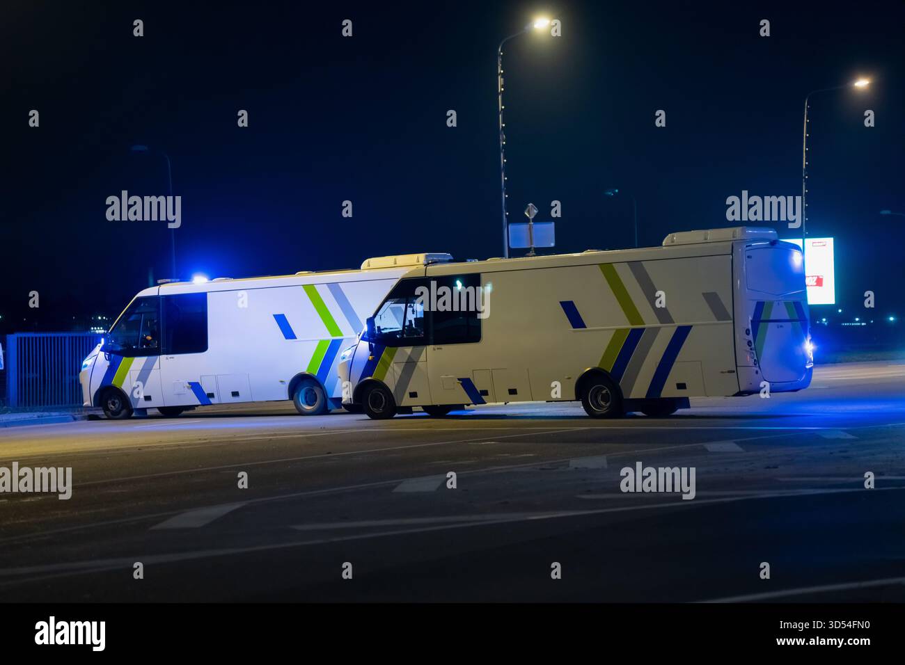 Pair of illuminated emergency service vans stationed on a dark roadway ...