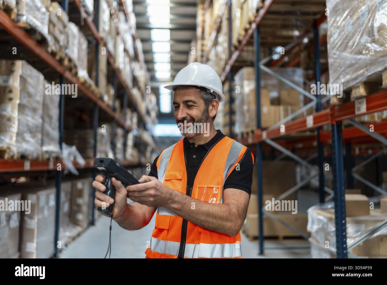 Male logistics worker wearing a hard hat and safety vest, scanning ...