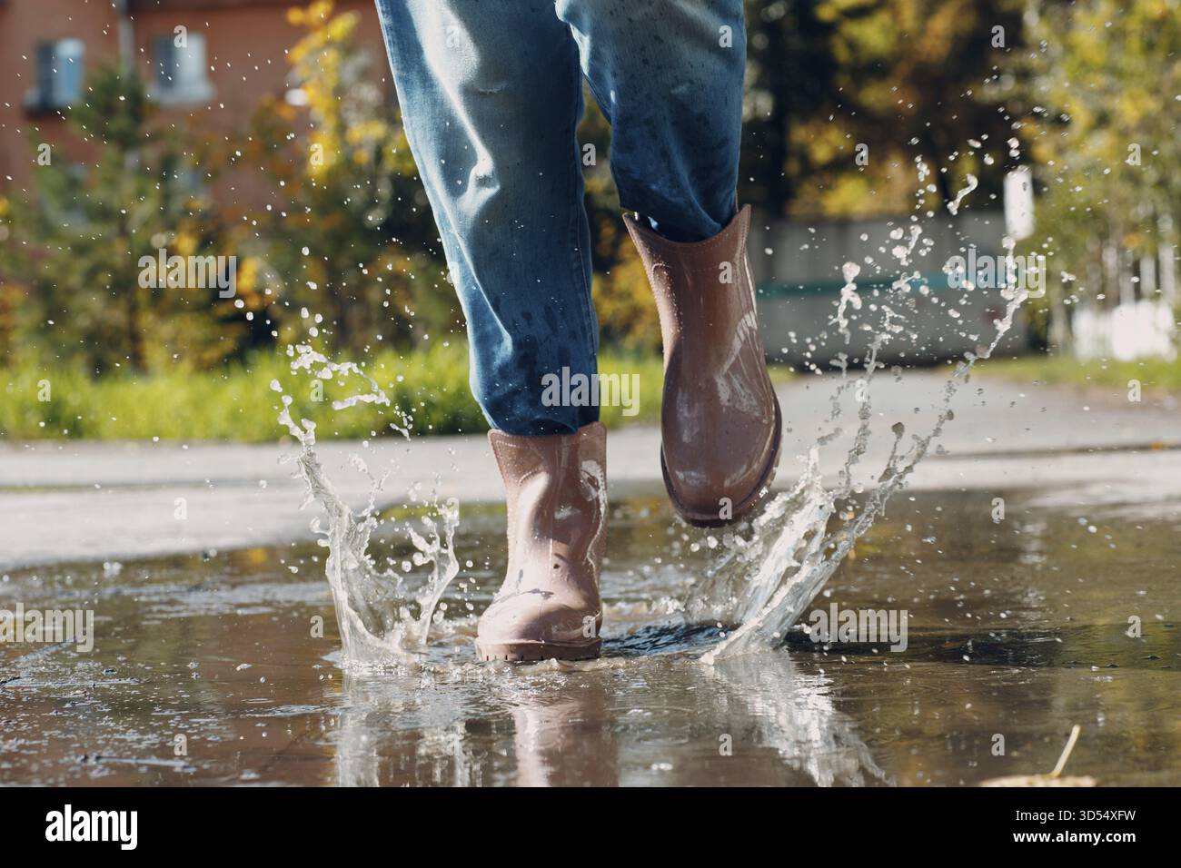 Woman wearing rain rubber boots walking running and jumping into puddle ...