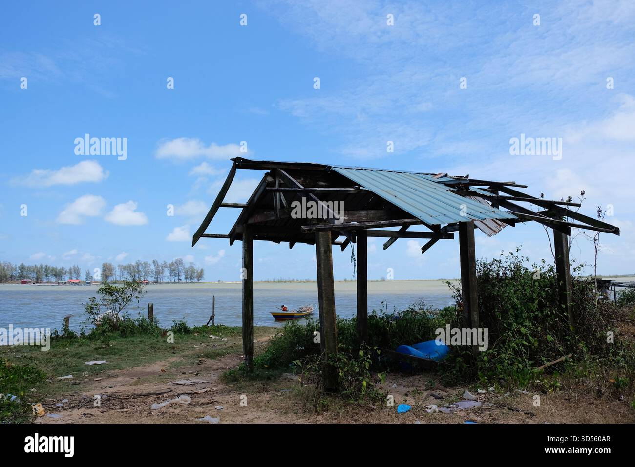 An old wooden shack with a rusty metal roof stands by the riverside ...