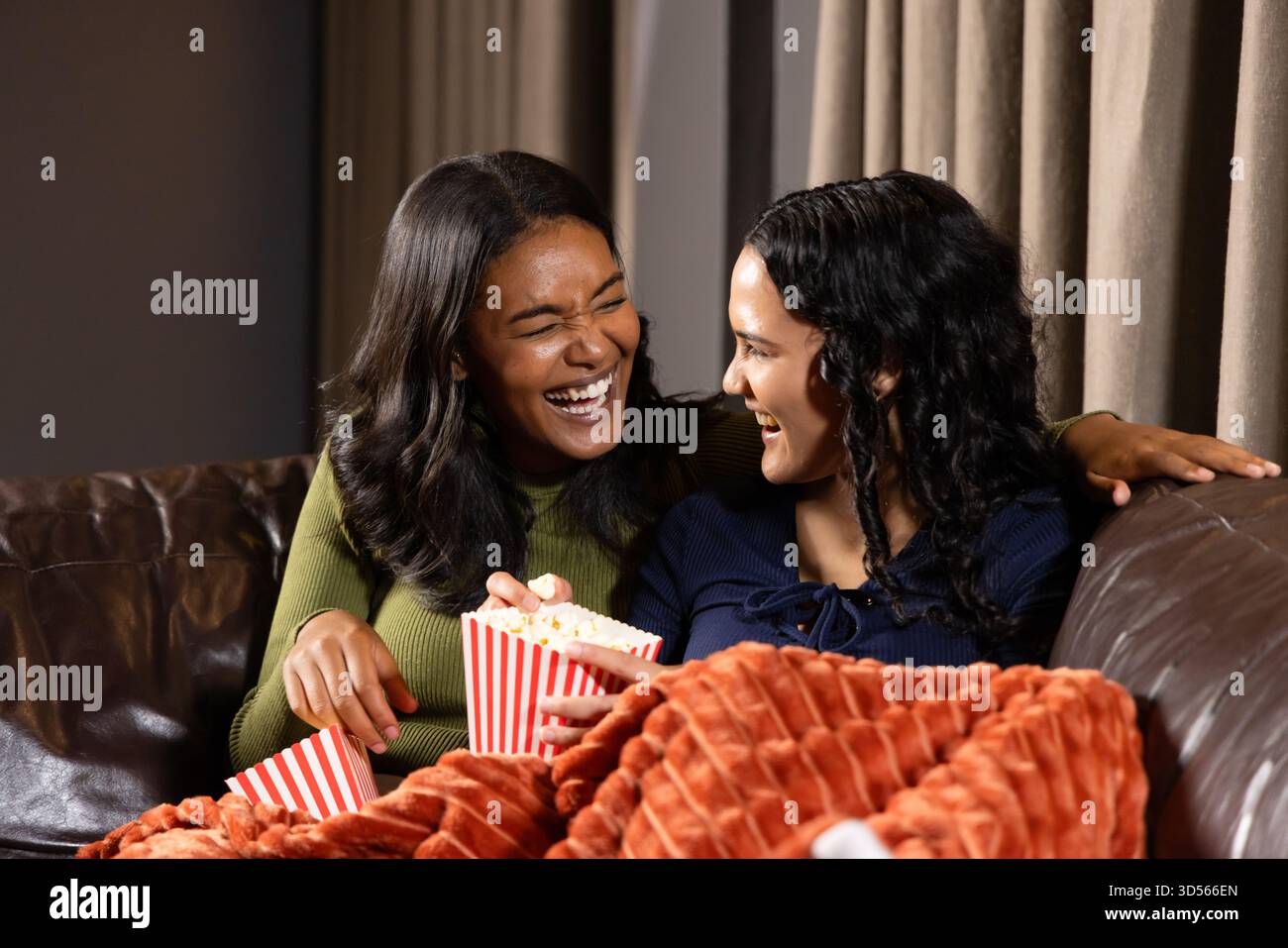 Laughing Diverse female friends snuggling on leather sofa at home, with ...
