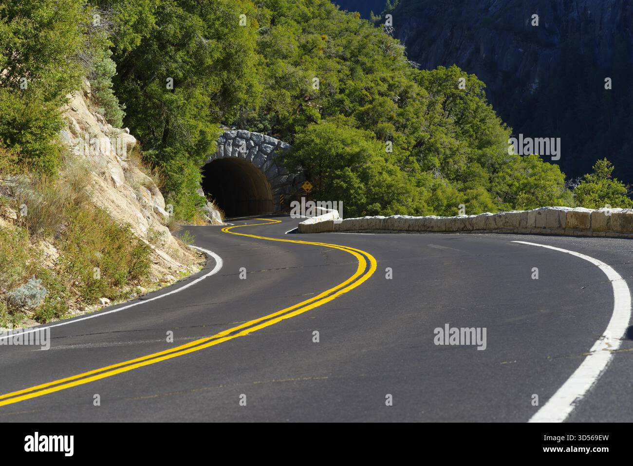Curvy road leading into a mountain tunnel under clear daylight. This is ...