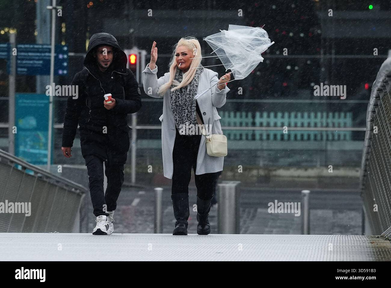 A person holding an umbrella crosses the Sean O'Casey bridge a wet and windy afternoon in Dublin ...