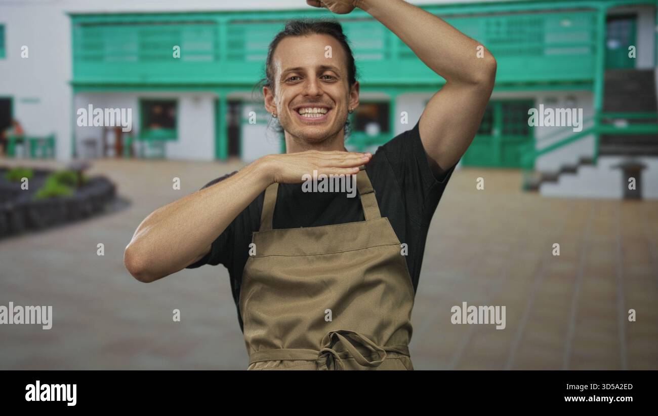 Man smiling with hands framing face at building entrance wearing apron ...