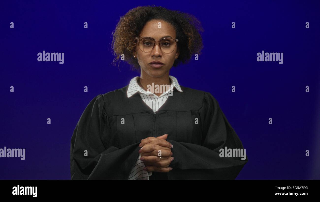 Woman judge wearing black robe with folded hands and glasses in studio ...