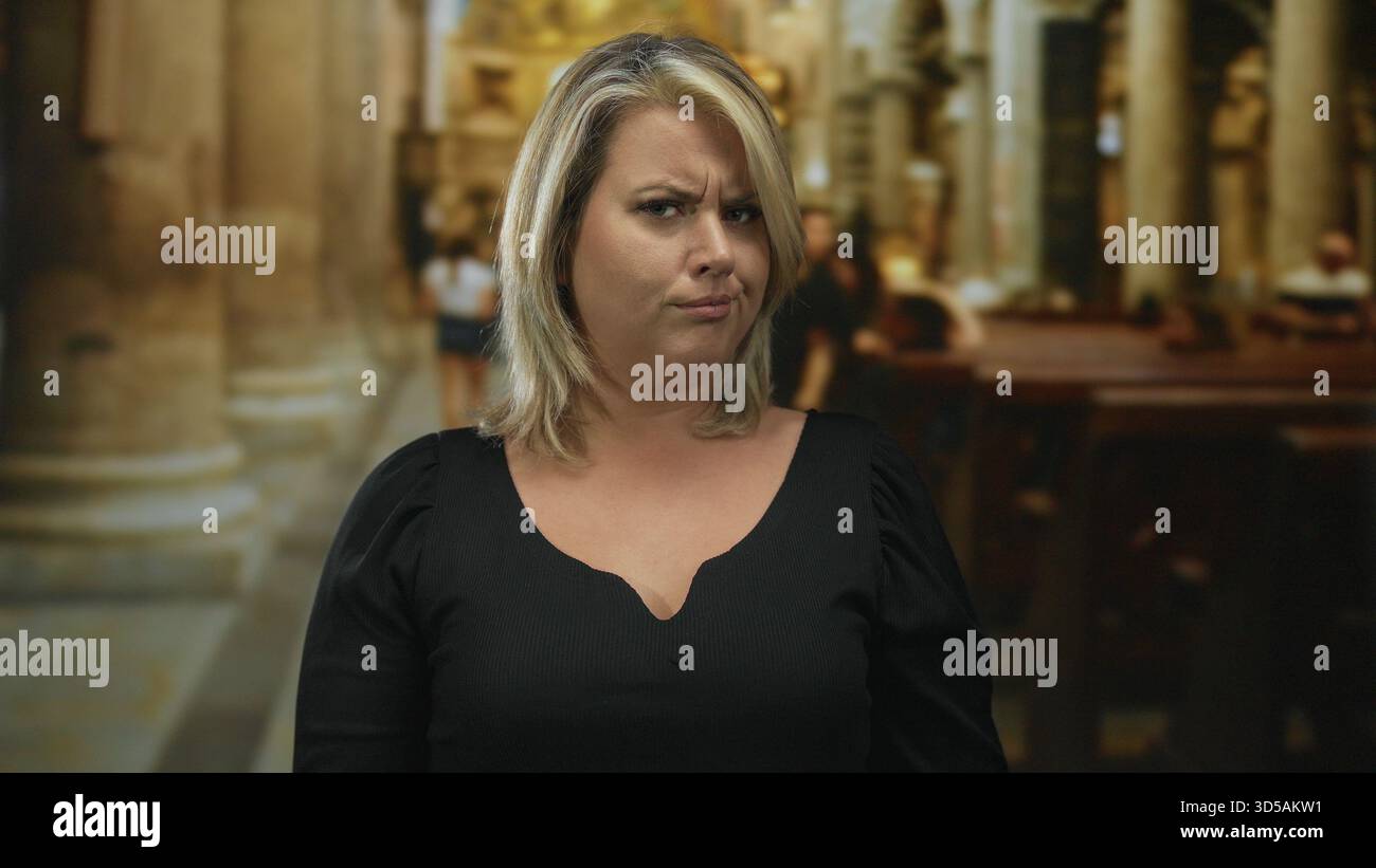 Blonde woman furrows eyebrows in building entrance with wooden pews and ...