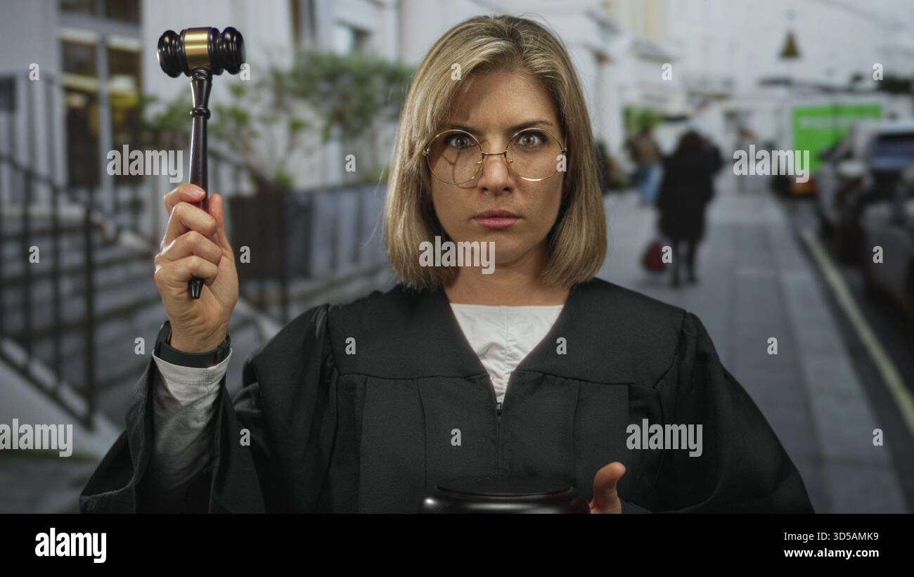 Serious woman judge in black robe holds wooden gavel aloft on bustling ...